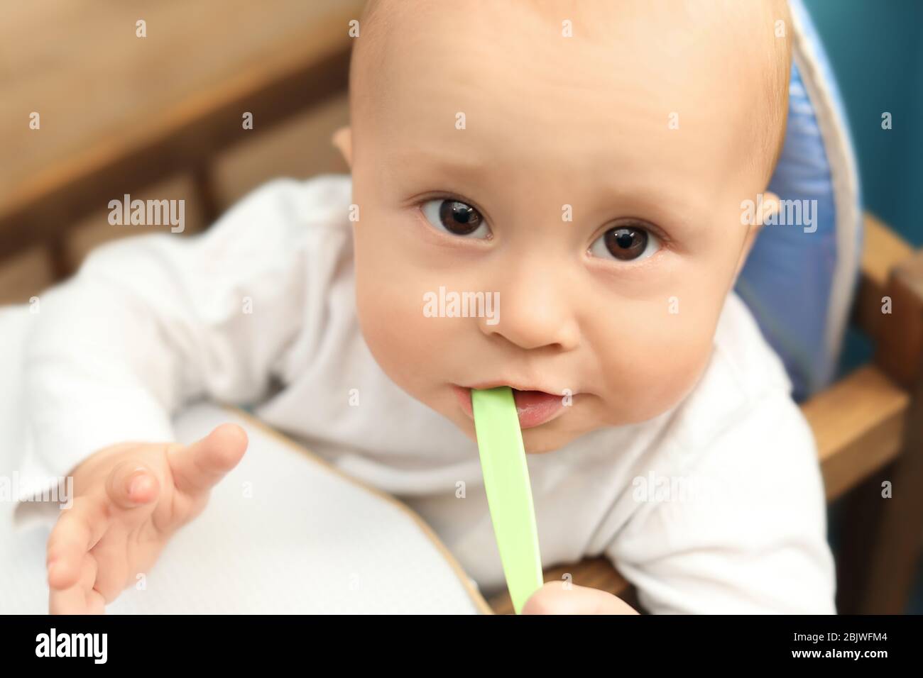 Cute baby with spoon sitting in kitchen Stock Photo - Alamy