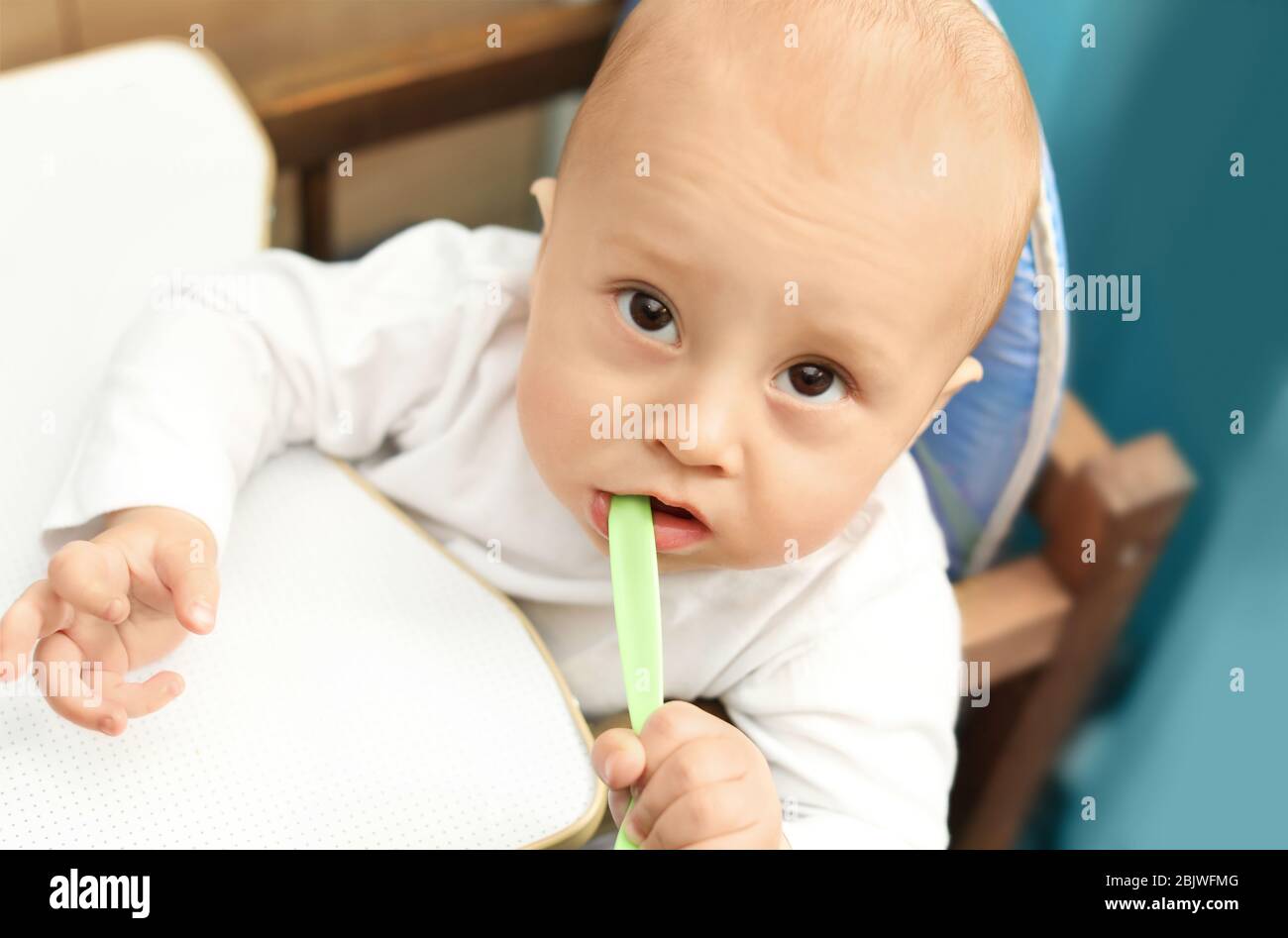 Cute baby with spoon sitting in kitchen Stock Photo - Alamy