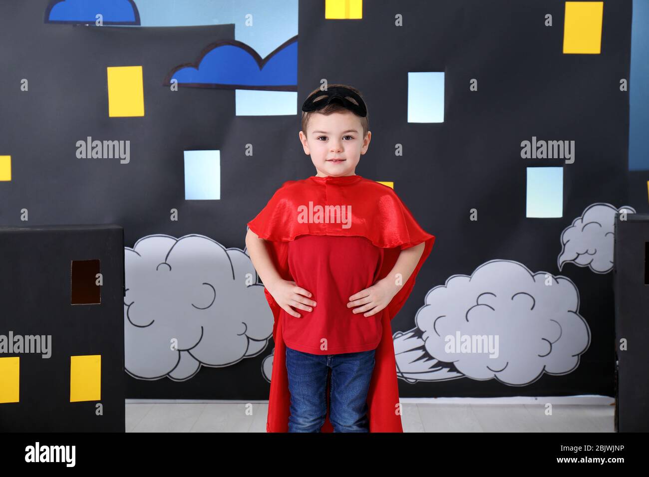 Cute boy in superhero costume against comic strip themed decoration ...