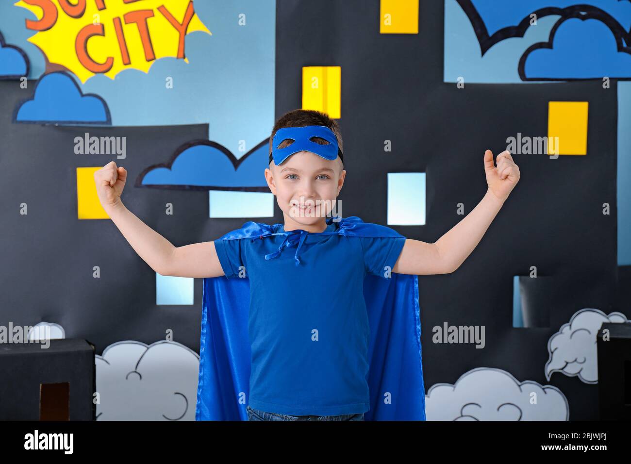 Cute boy in superhero costume against comic strip themed decoration ...