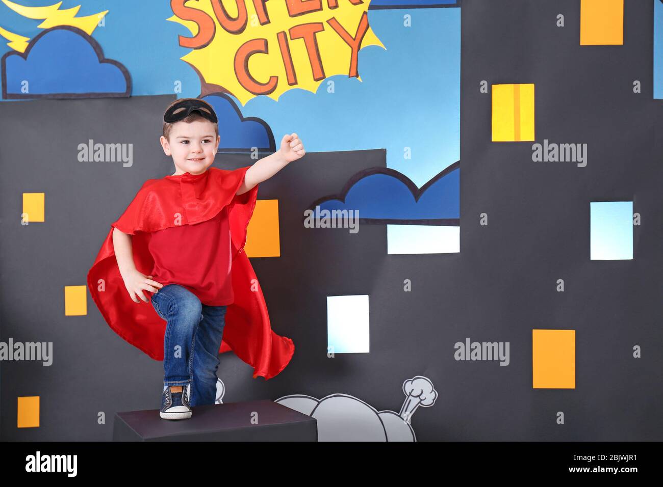 Cute boy in superhero costume against comic strip themed decoration ...