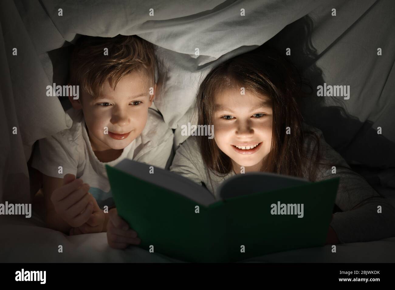 Cute little brother and sister reading bedtime story under blanket in ...