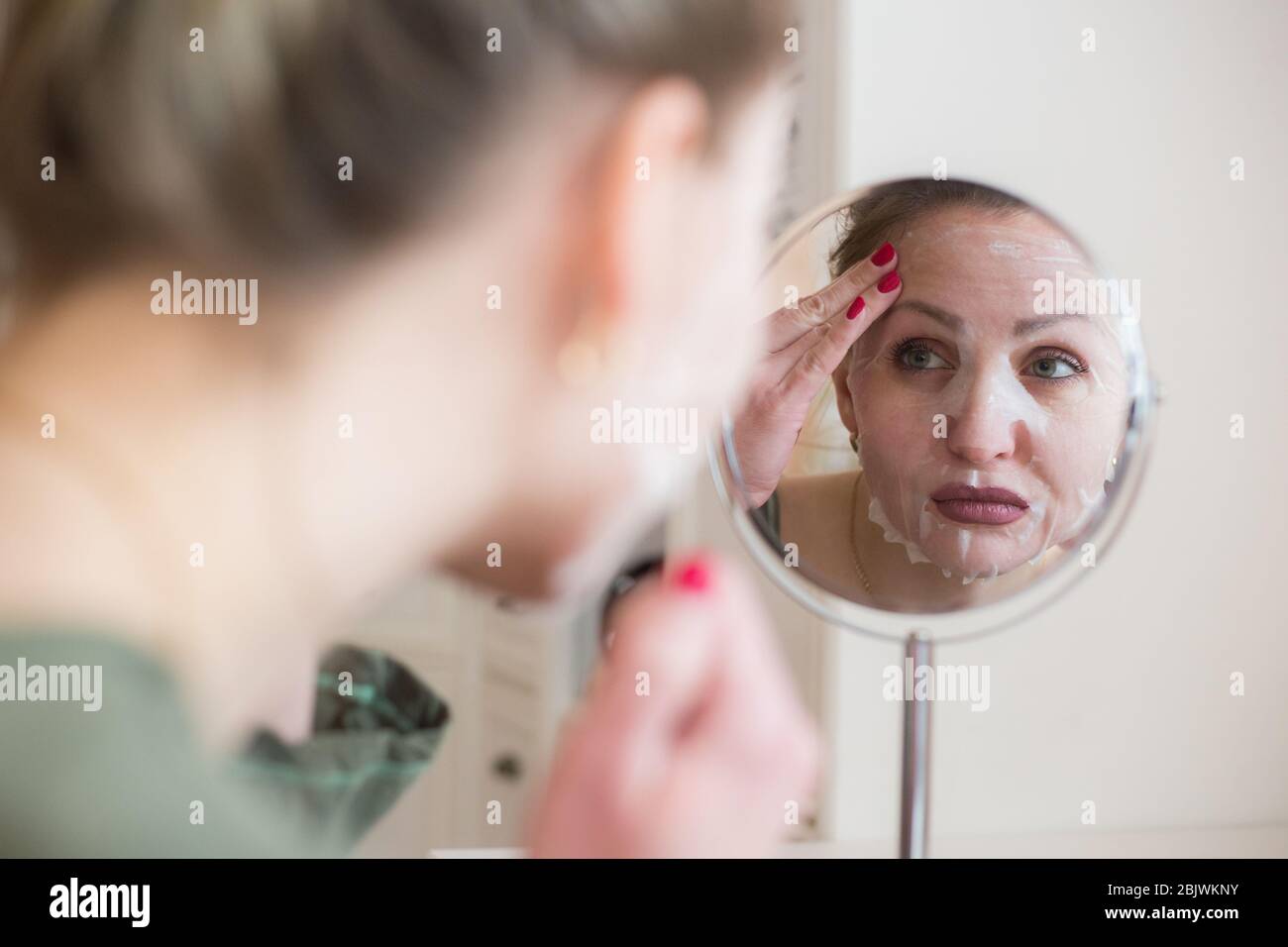Cosmetic face mask and girl look in the mirror Stock Photo - Alamy