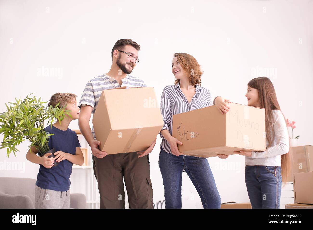 Couple with children carrying boxes indoors. Happy family on moving day ...