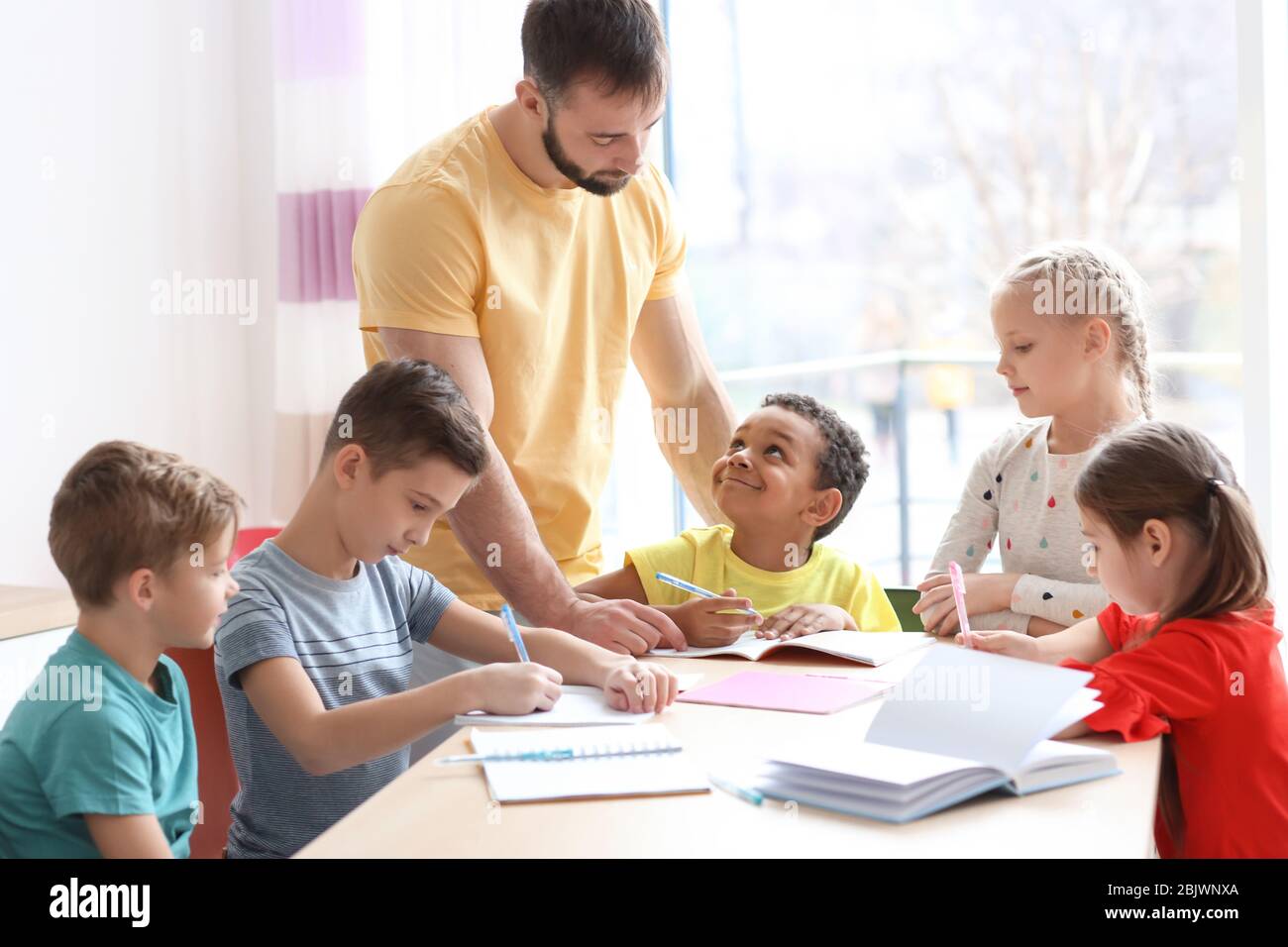 Male teacher helping children with homework in classroom at school ...