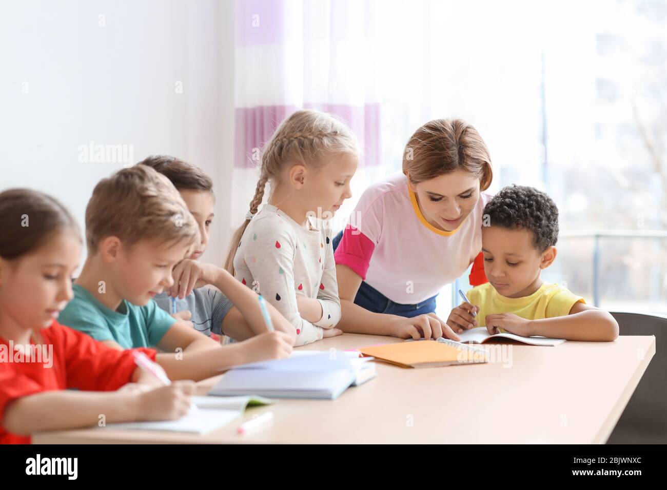 Female teacher helping children with homework in classroom at school ...