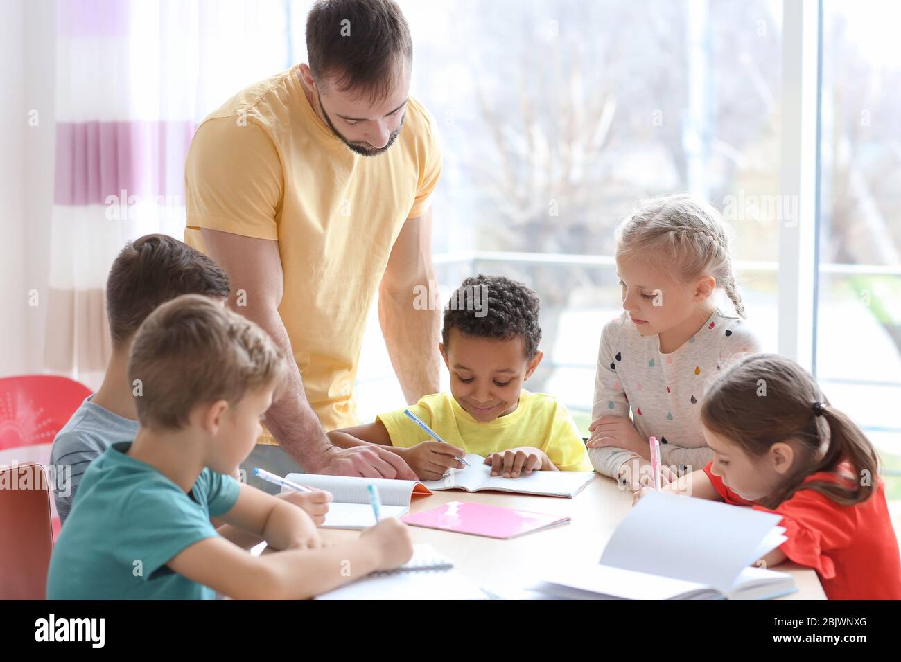Male teacher helping children with homework in classroom at school ...