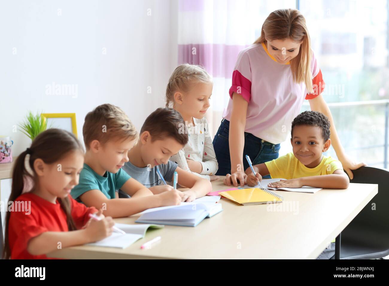Female teacher helping children with homework in classroom at school ...