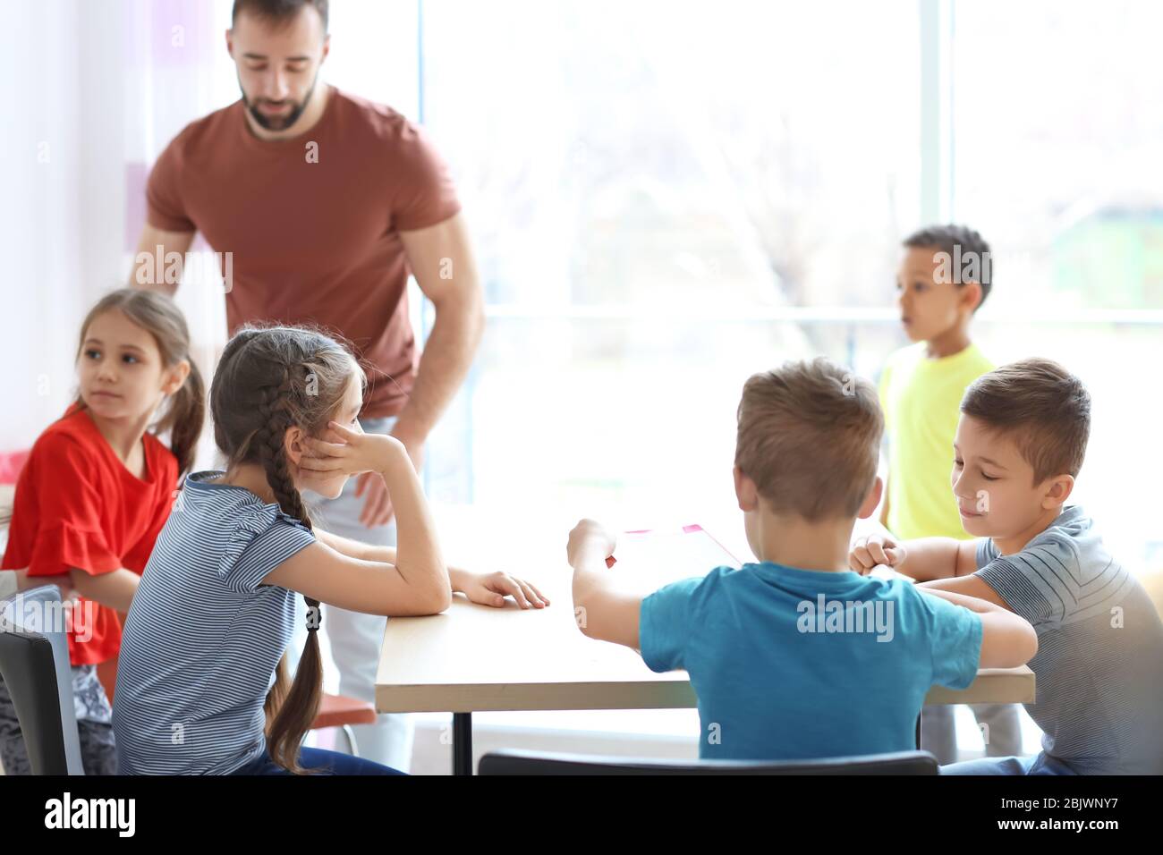 Male teacher helping children with homework in classroom at school ...