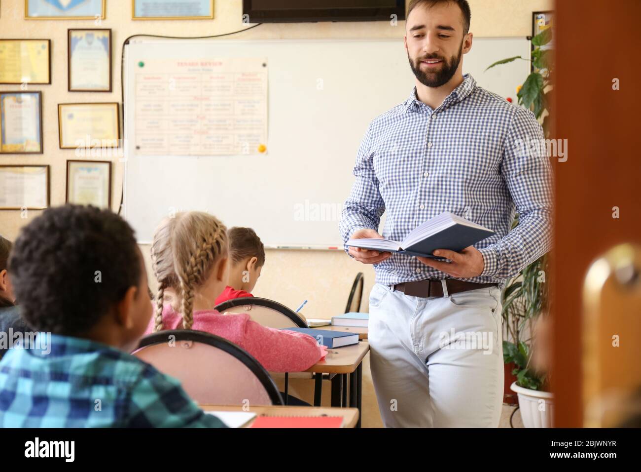 Male teacher helping children with homework in classroom at school ...