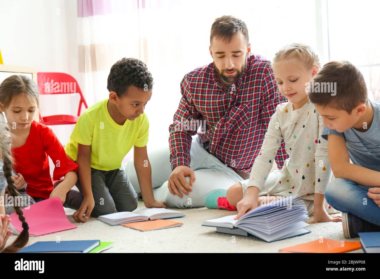 Male teacher helping children with homework in classroom at school ...