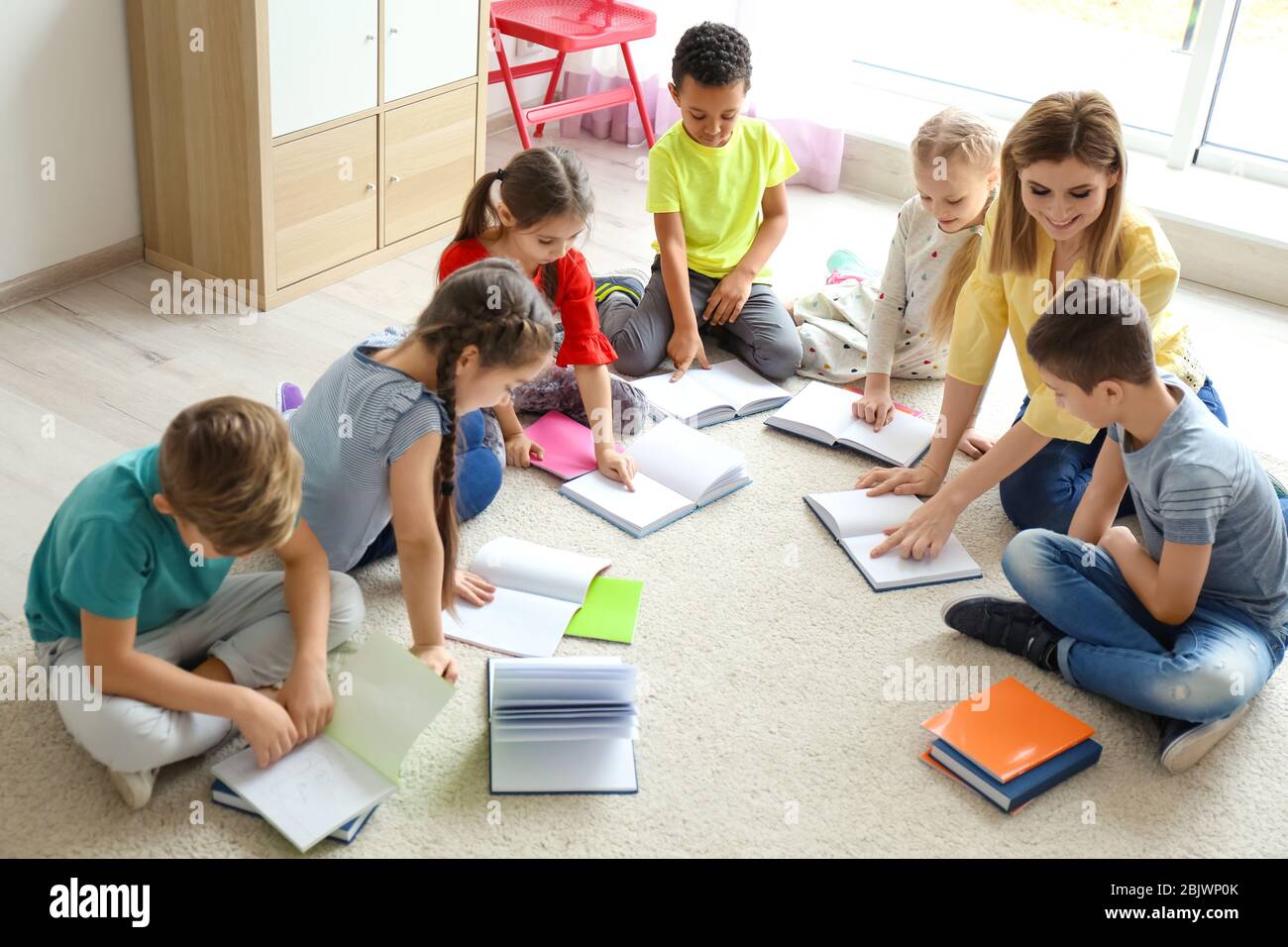 Female teacher helping children with homework in classroom at school ...