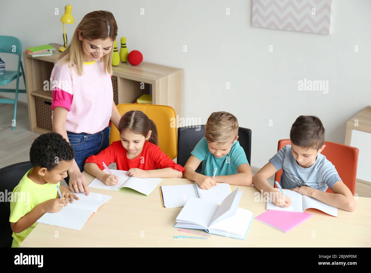Female teacher helping children with homework in classroom at school ...