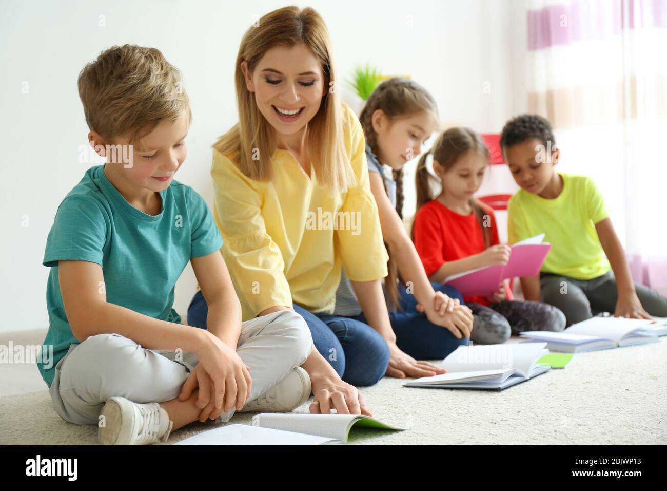 Female teacher helping children with homework in classroom at school ...