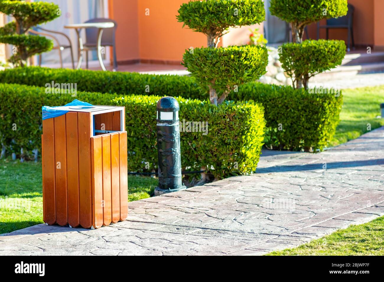 Yellow wooden trash can outdoors on the side of sidewalk in park ...