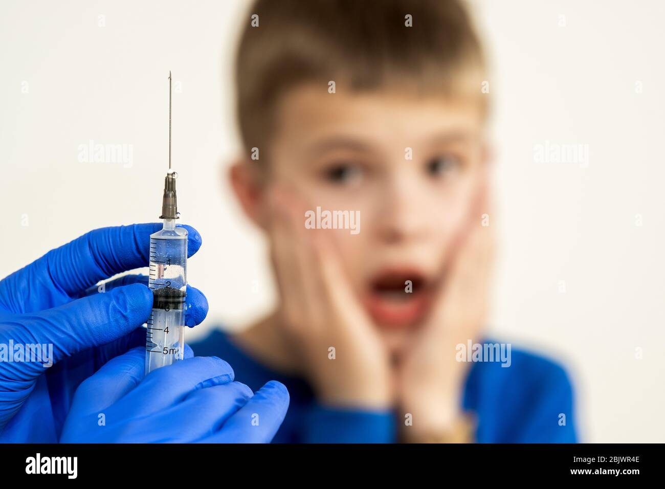Doctor preparing vaccination injection with a syringe to an afraid ...