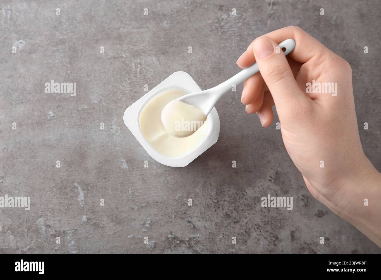 Woman eating tasty yogurt at grey table Stock Photo - Alamy