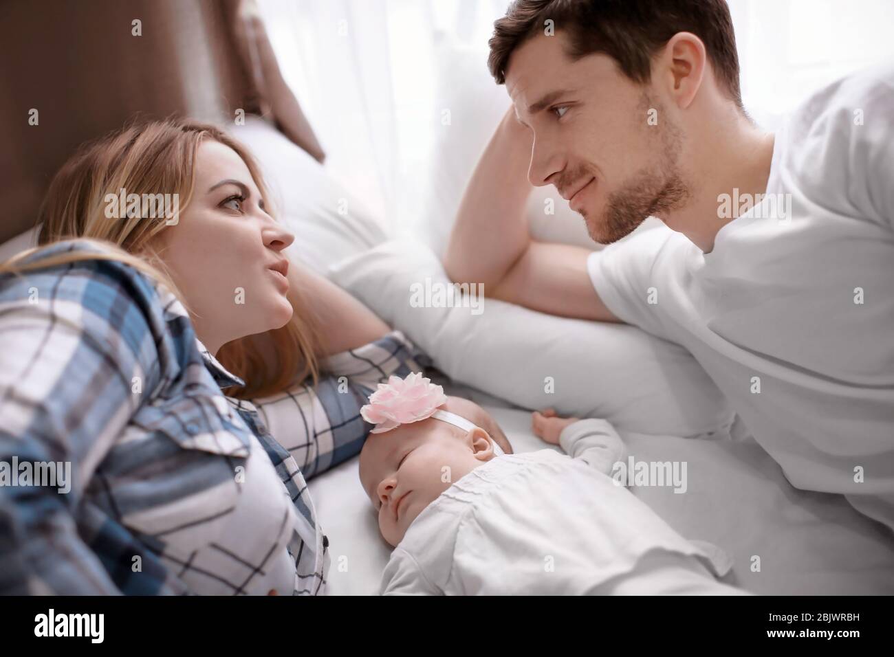 Young parents with cute sleeping baby on bed at home Stock Photo - Alamy