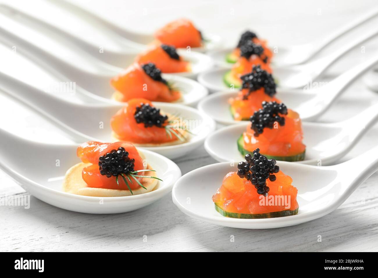 Tasty appetizers with black caviar and salmon in ceramic spoons on ...