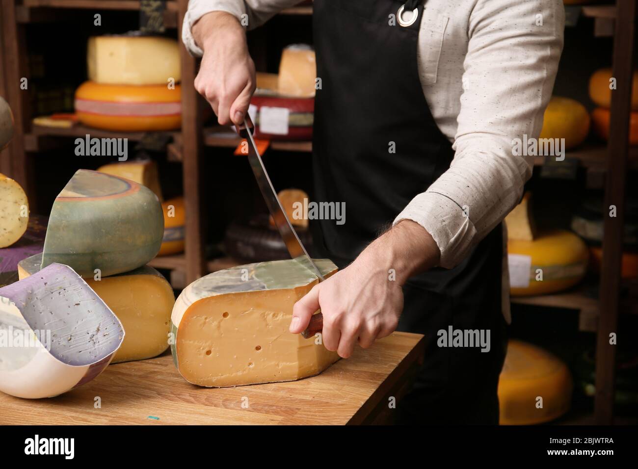 Young worker cutting cheese in shop Stock Photo - Alamy