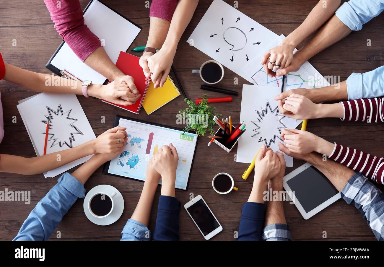 Young people holding hands while working on project at table. Unity ...