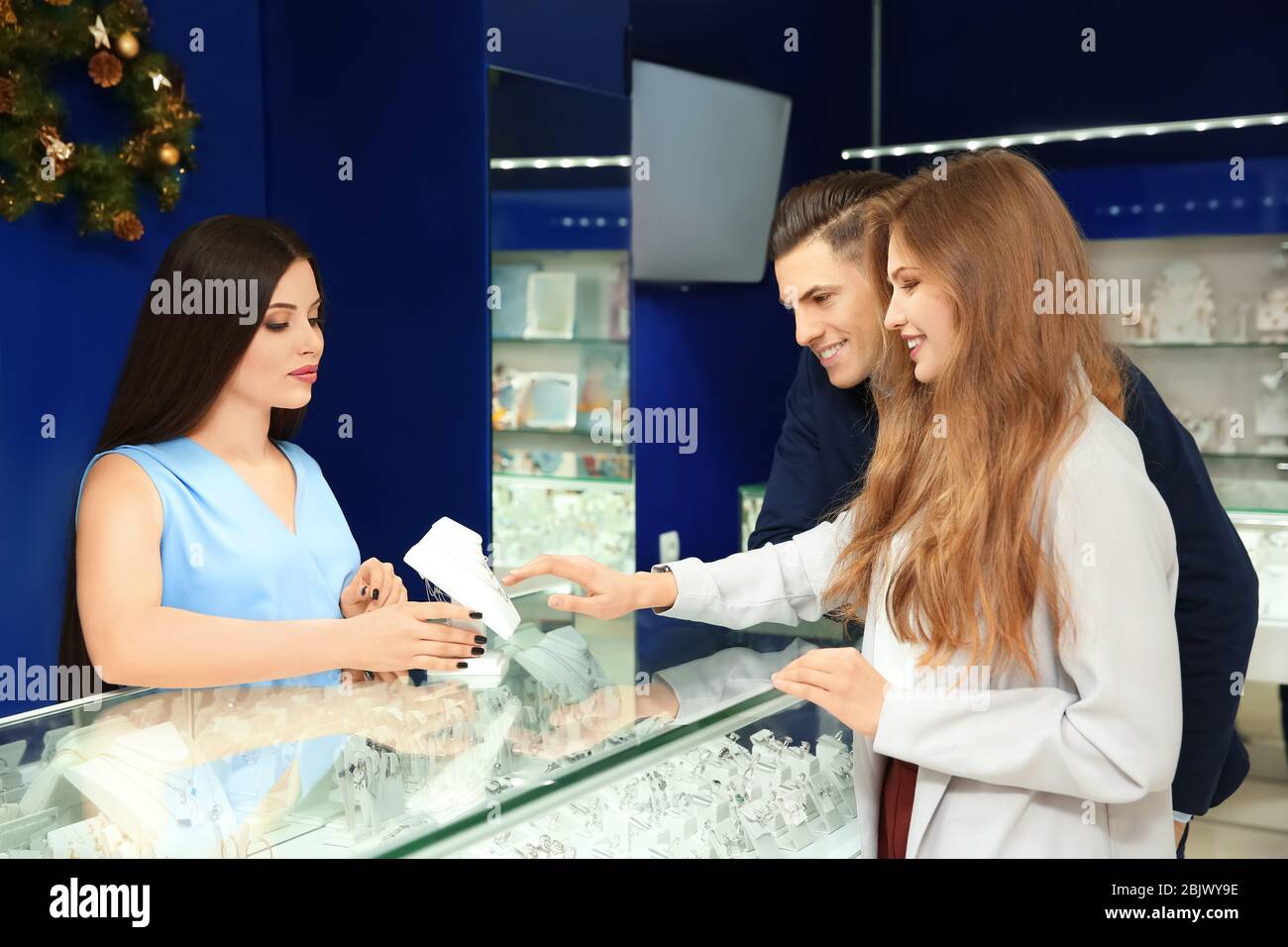 Young shop assistant helping couple choose necklace in jewelry store ...