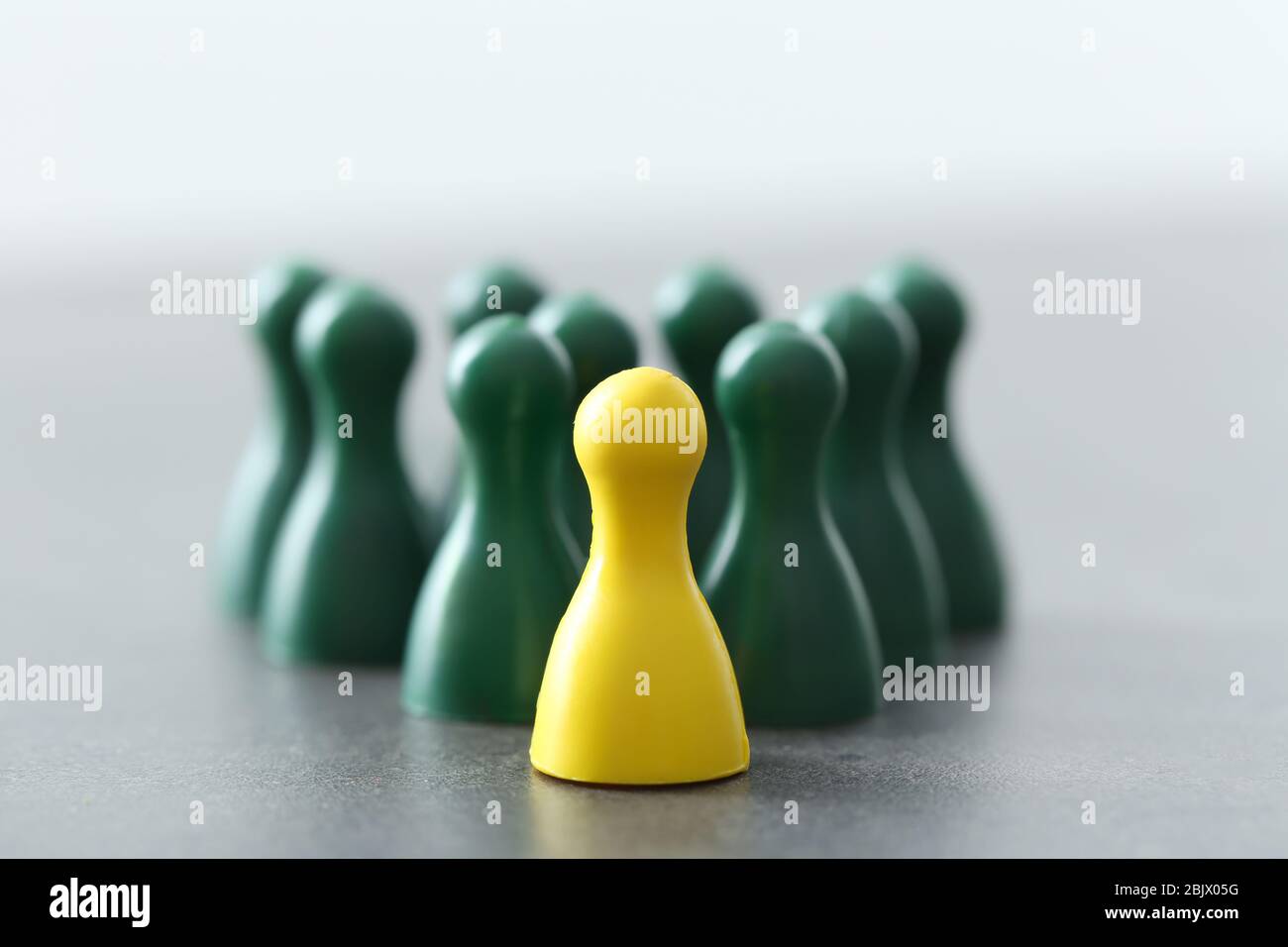 Yellow pawn among green ones on gray table. Difference and uniqueness ...