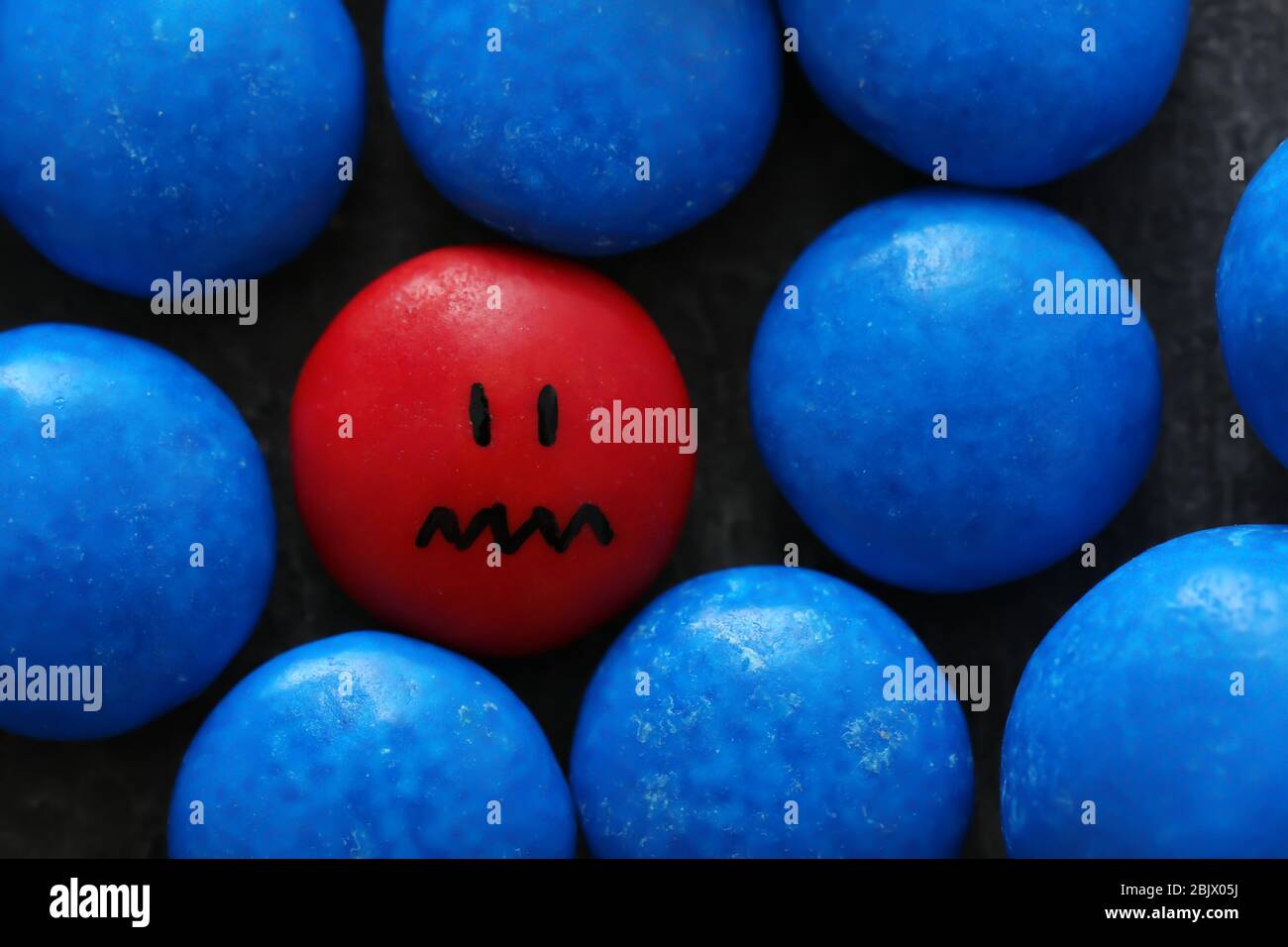 One red drop with painted sad face among blue ones. Difference and ...