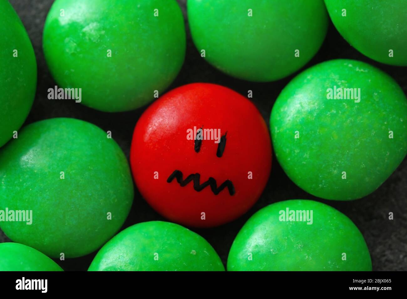 One red drop with painted sad face among green ones. Difference and ...