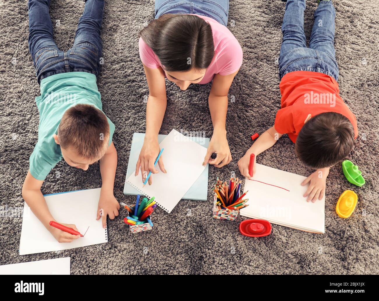 Two little boys drawing with nanny at home Stock Photo - Alamy