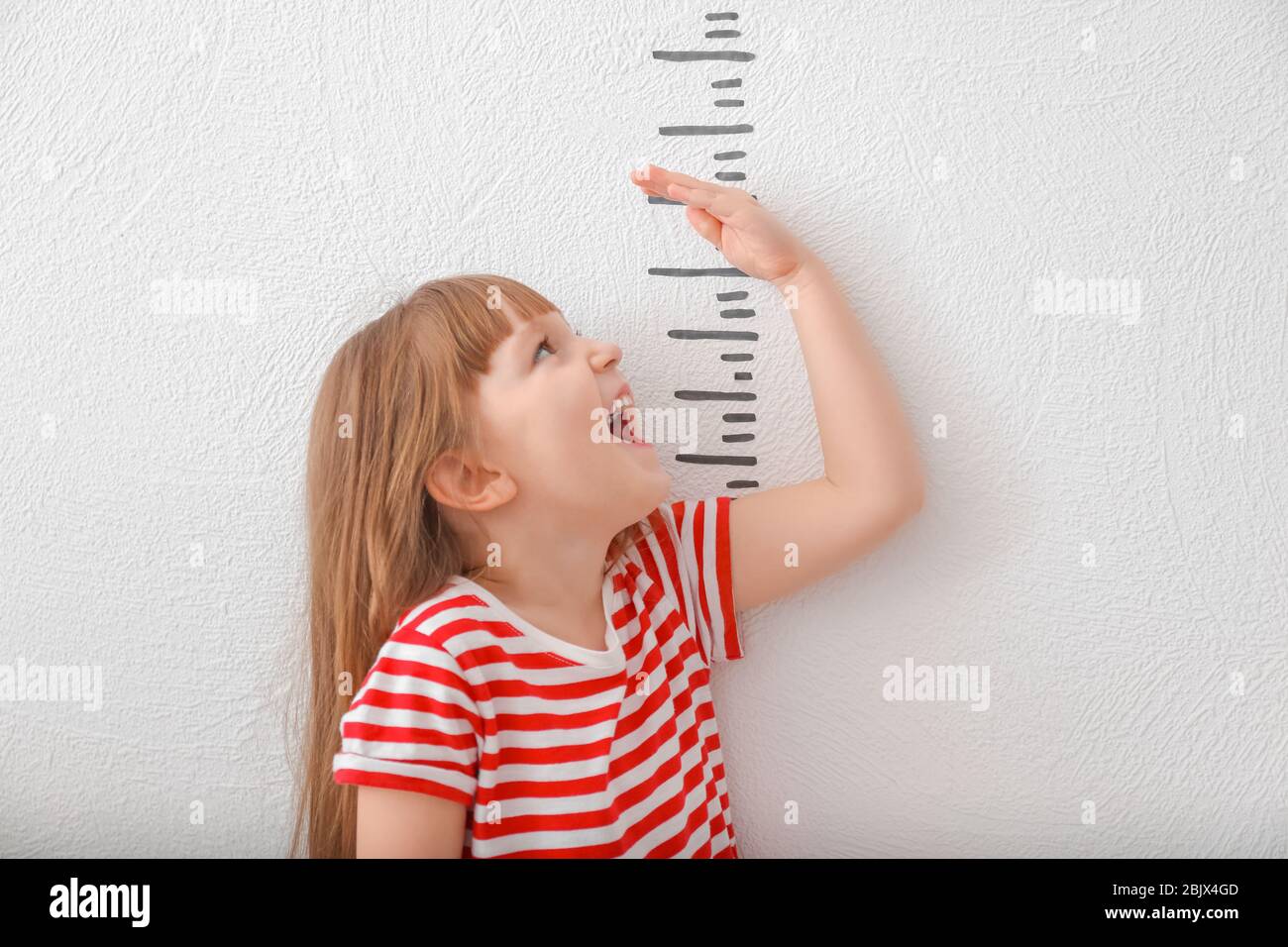 Cute little girl measuring height on light background Stock Photo - Alamy