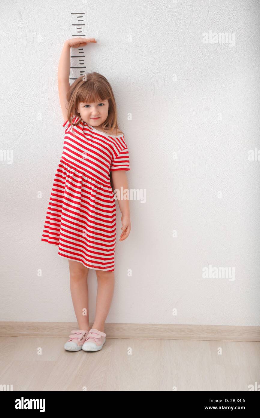 Cute little girl measuring height near light wall Stock Photo - Alamy