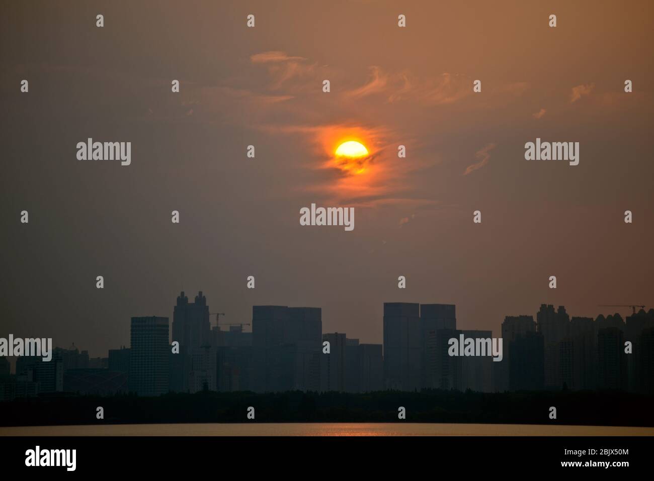 Wuhan: Sunset over the city skyline from the East Lake, with smog and a ...