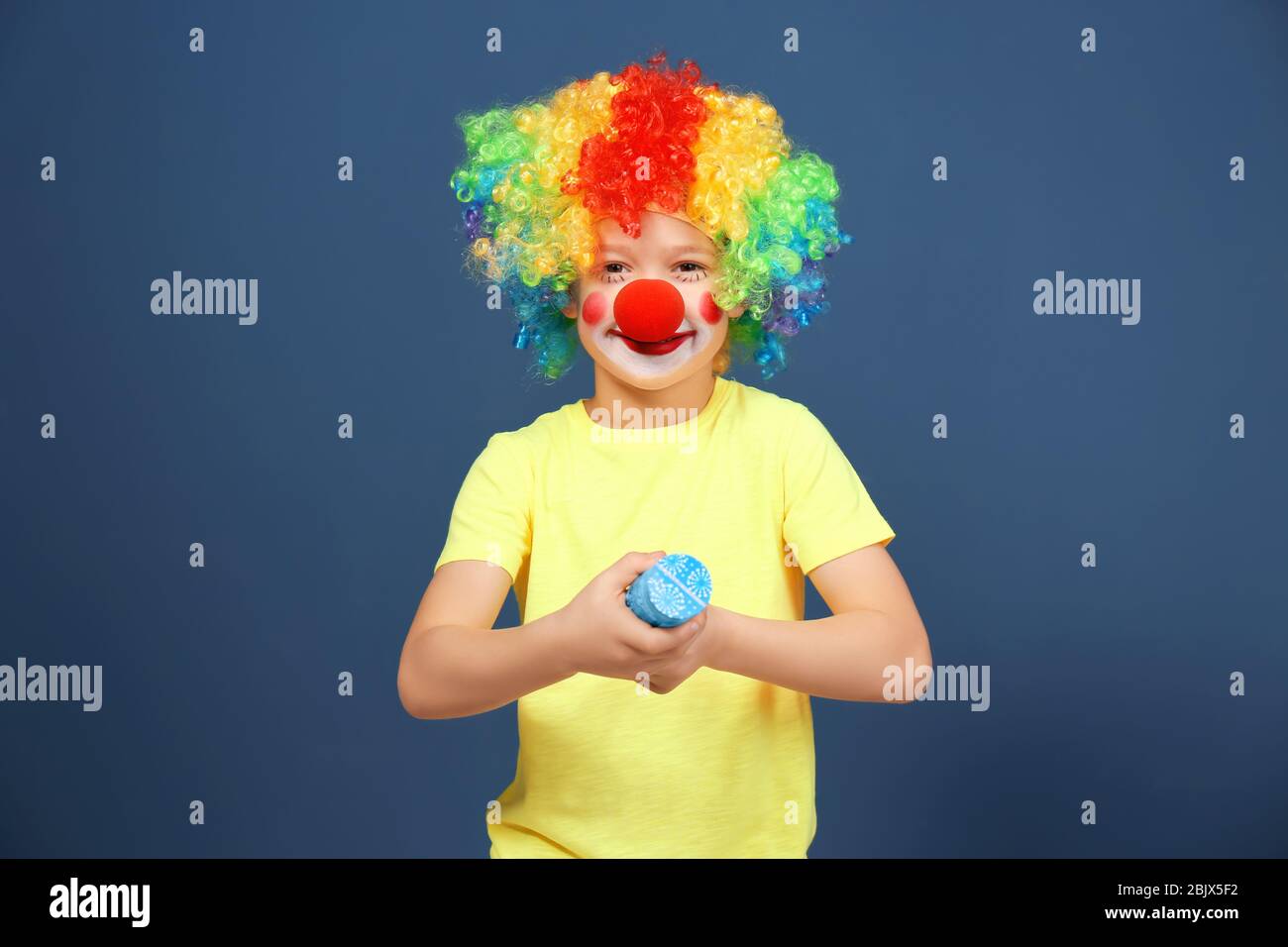Cute little boy with clown makeup and party popper on color background ...
