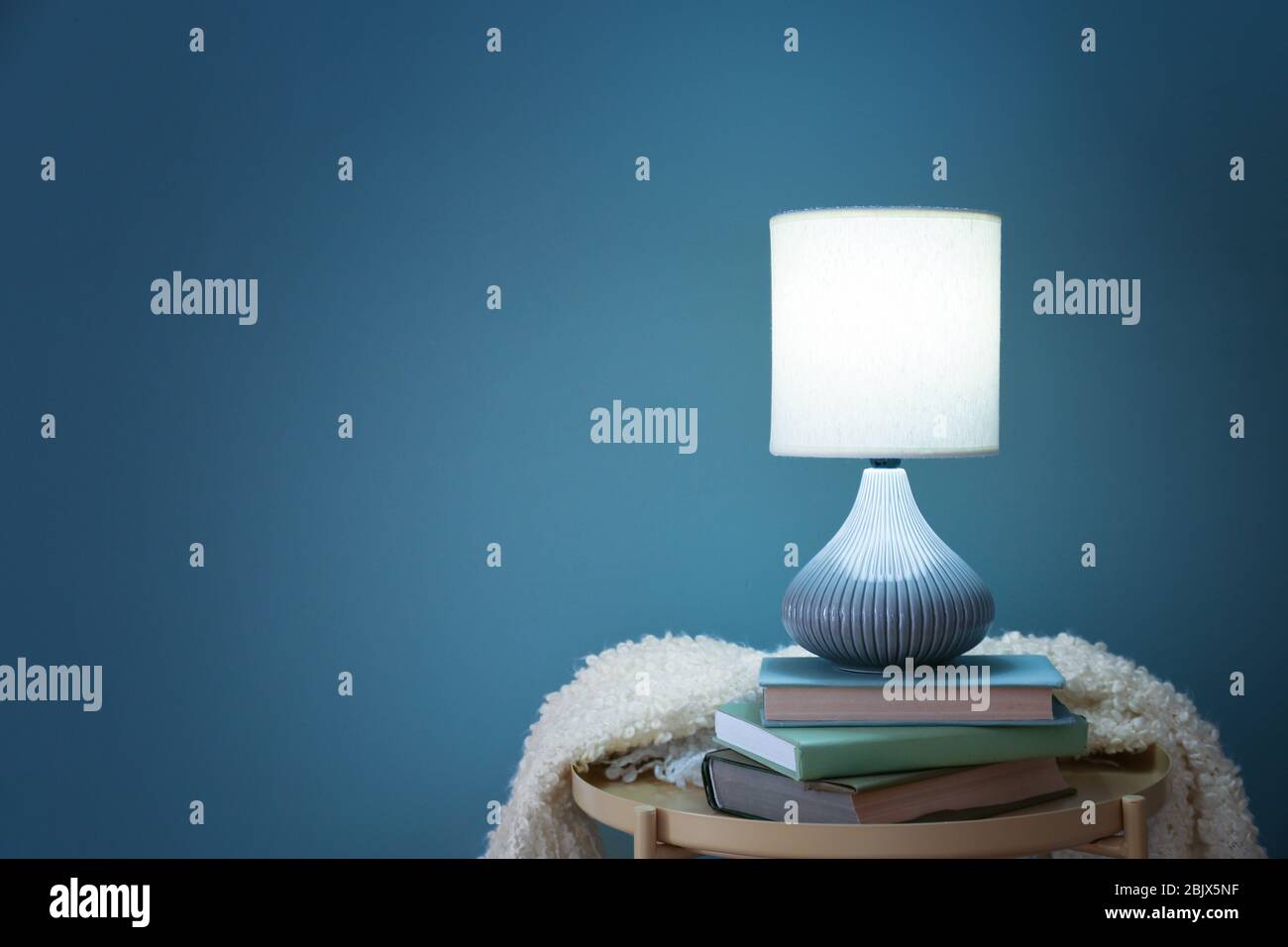 Elegant lamp on stack of books near color wall Stock Photo - Alamy