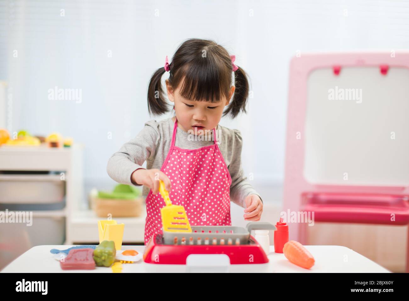 toddler girl pretend play food preparing role at home agianst white ...