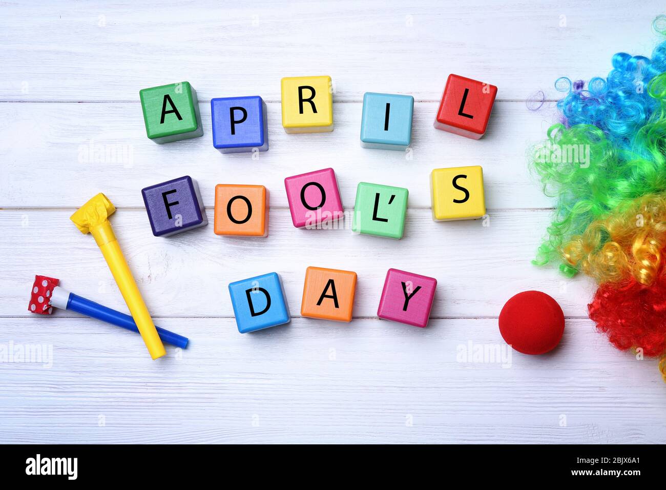 Party horns, cubes and rainbow wig on wooden background. April fool's ...