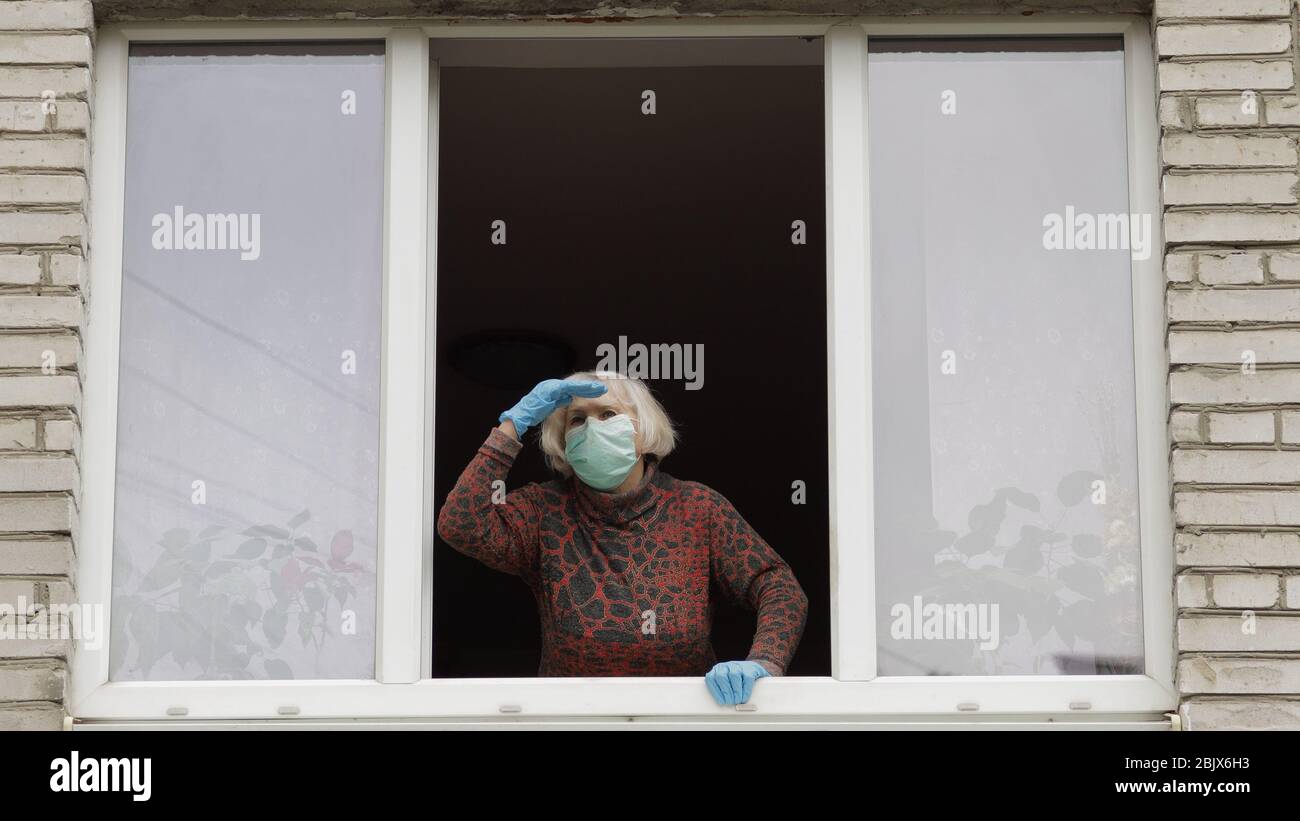Old woman stay at window in protection mask. Isolated at home on ...