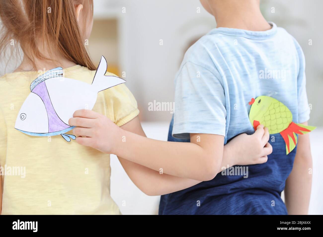 Little children sticking paper fish on each other indoors. April fool's ...