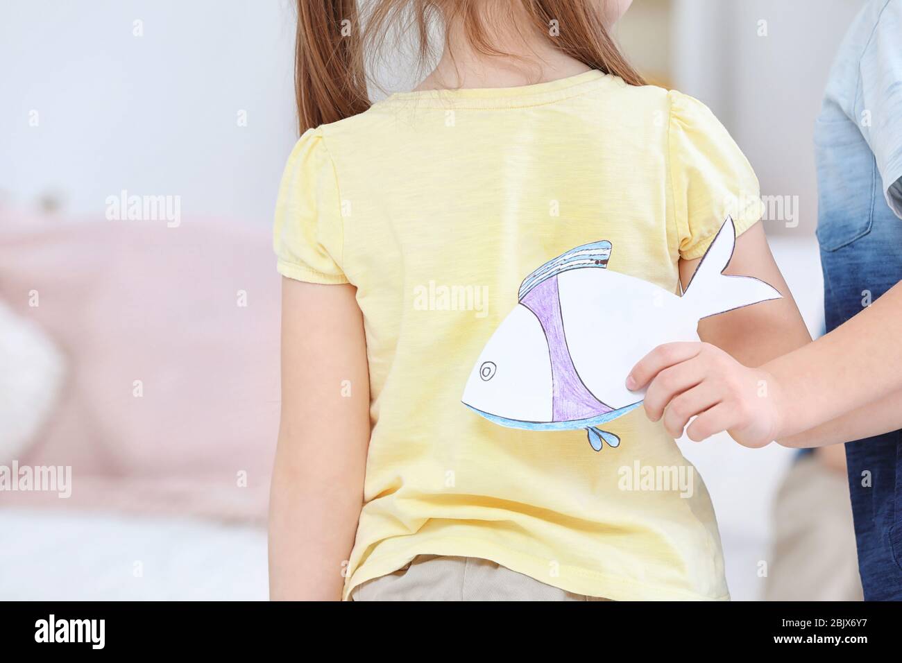 Little boy sticking paper fish to girl's back indoors. April fool's day ...