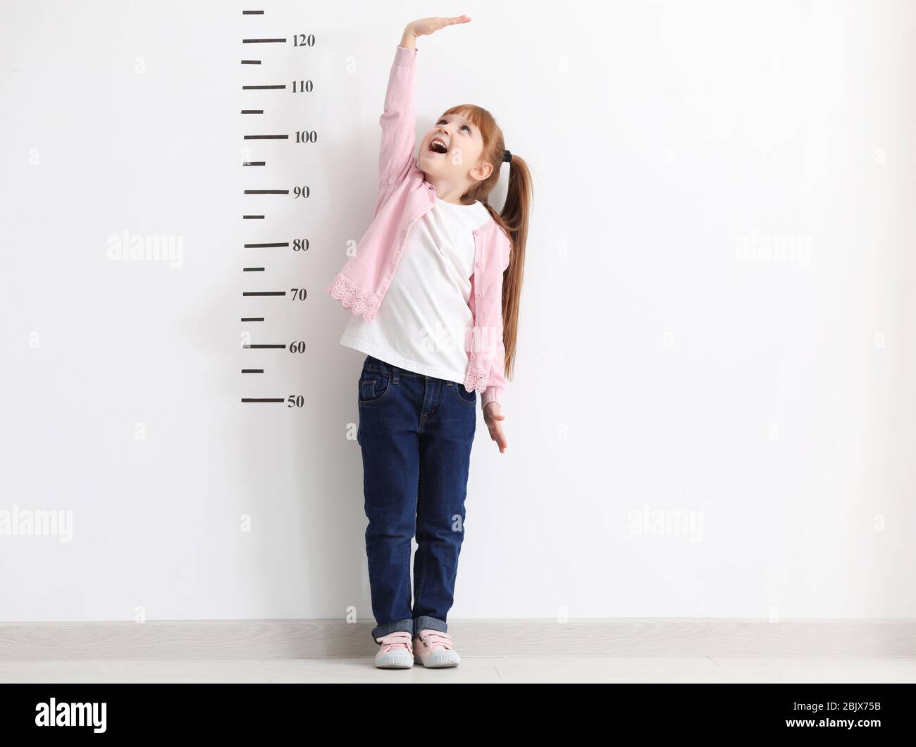 Little girl measuring height near white wall Stock Photo - Alamy