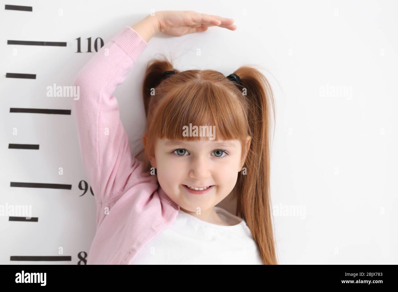 Little girl measuring height near white wall Stock Photo - Alamy