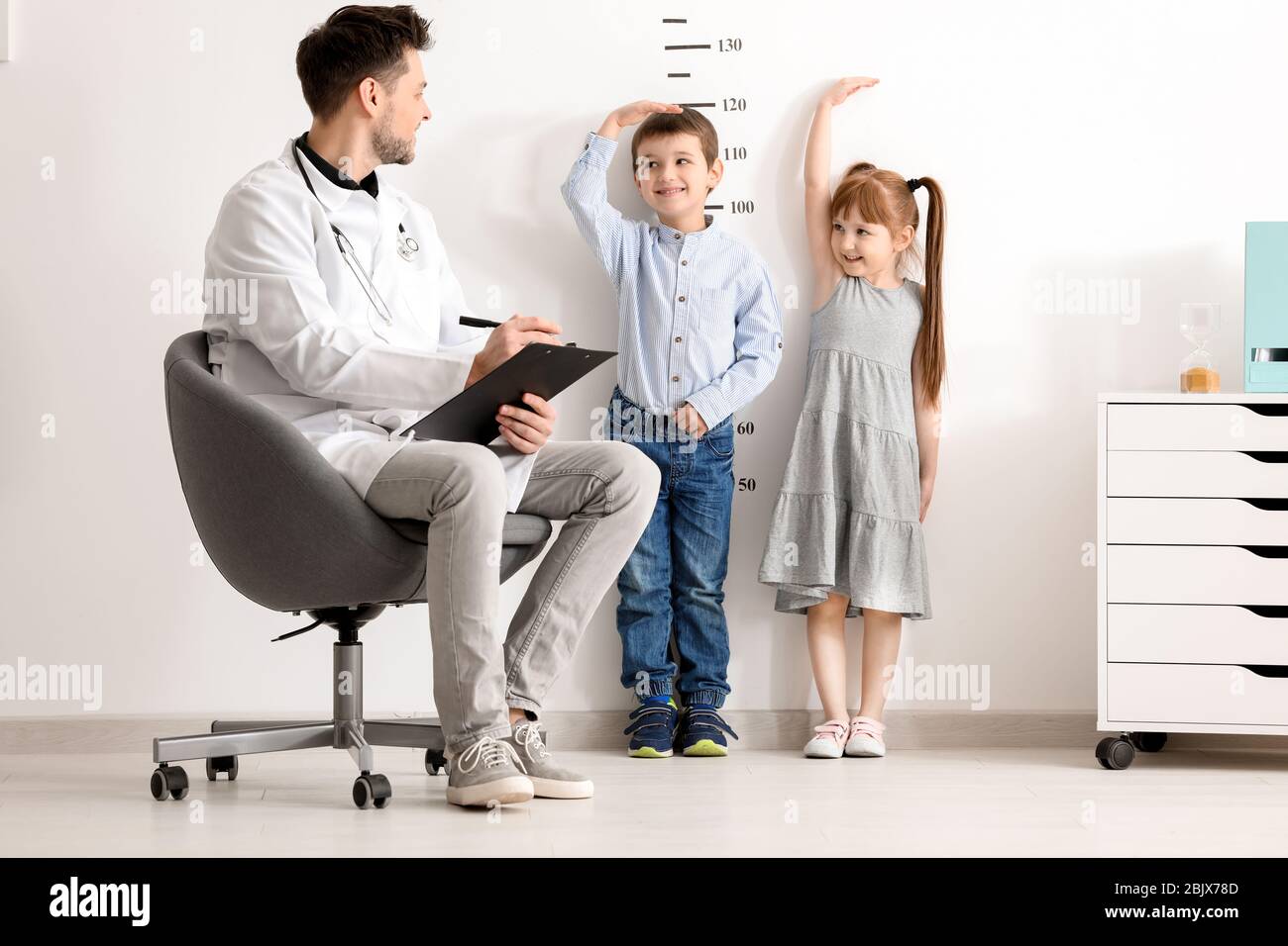 Male doctor measuring height of little children in clinic Stock Photo ...