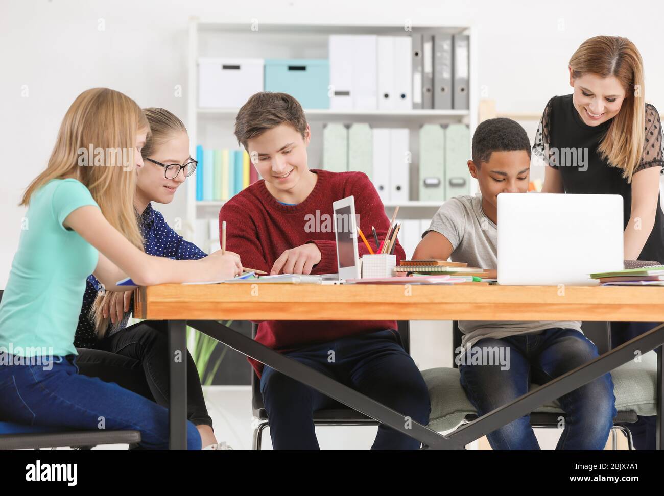 Group of teenagers doing homework with teacher in classroom Stock Photo ...