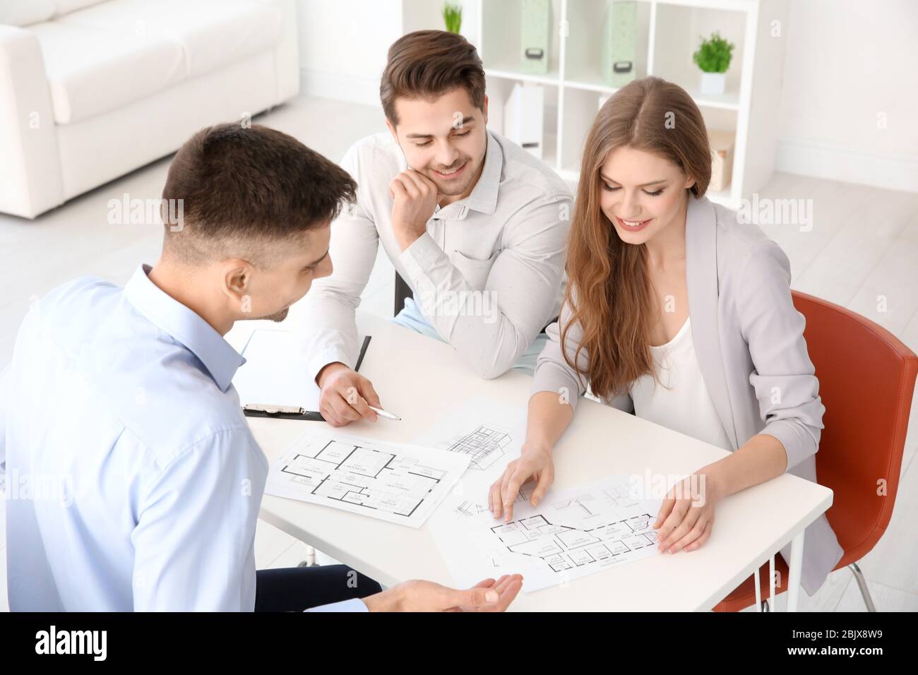 Real estate agent showing plan of apartment to clients in office Stock ...