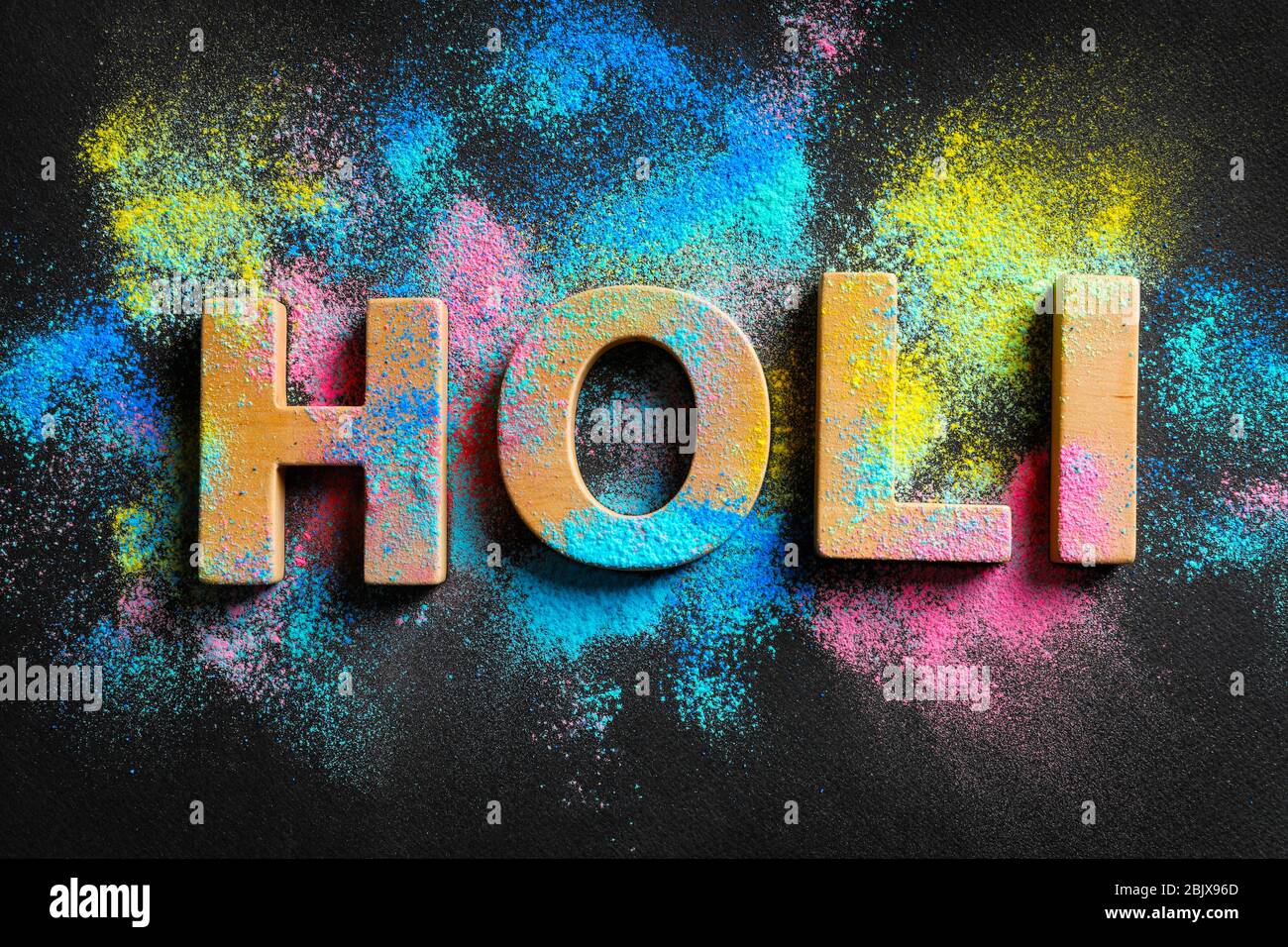 Word "HOLI" made of wooden letters and colorful powders on dark ...