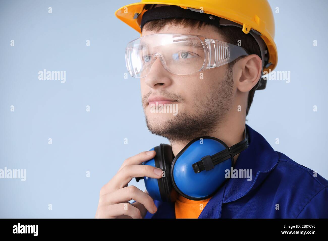 Male worker with headphones on grey background. Hearing protection ...