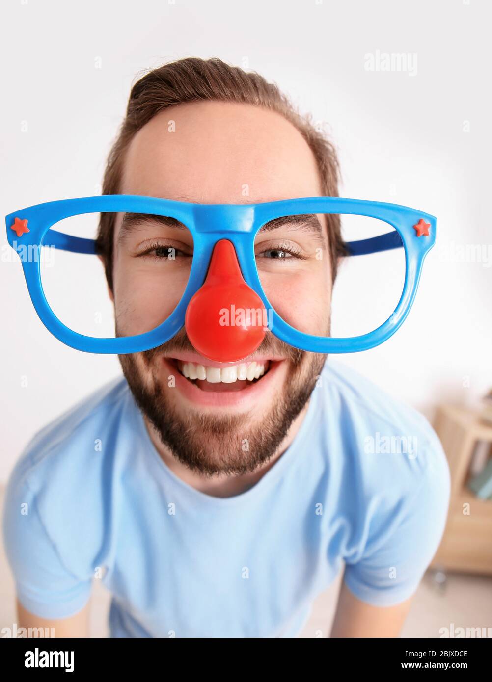 Young man in funny disguise posing on light background. April fool's ...