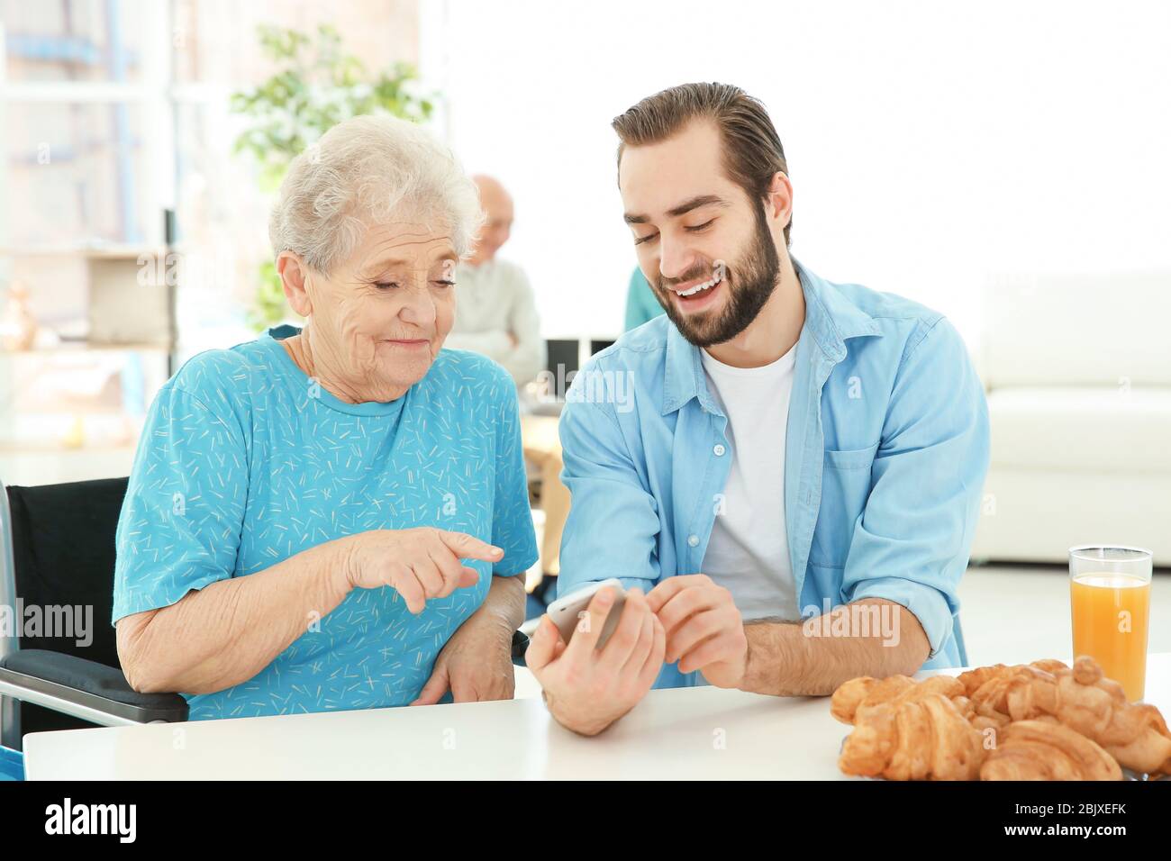 Young caregiver teaching senior woman to handle with mobile phone at ...