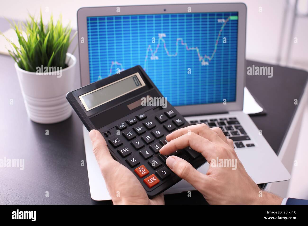 Man using calculator near laptop with stock chart data on screen. Forex ...